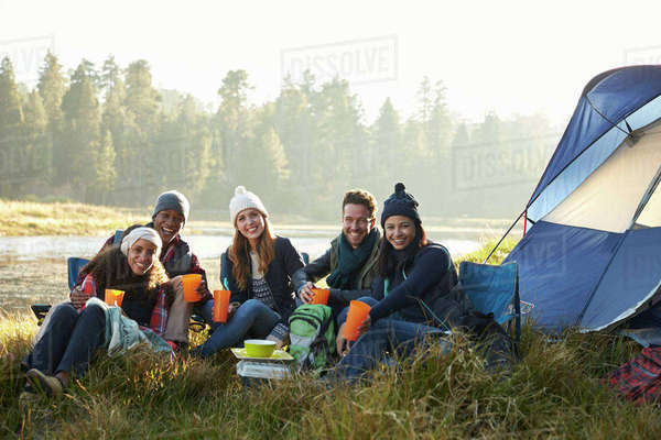 Friends sitting outside a tent near a lake looking to camera - Royalty ...