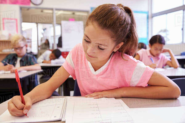 Schoolgirl writing at her desk in an elementary school class - Royalty ...
