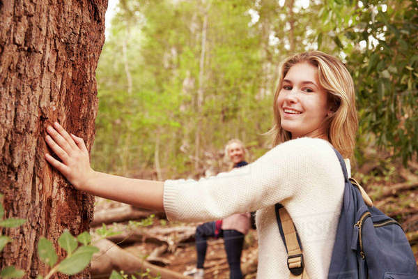 Girl touching a tree in a forest, her mother in the background ...