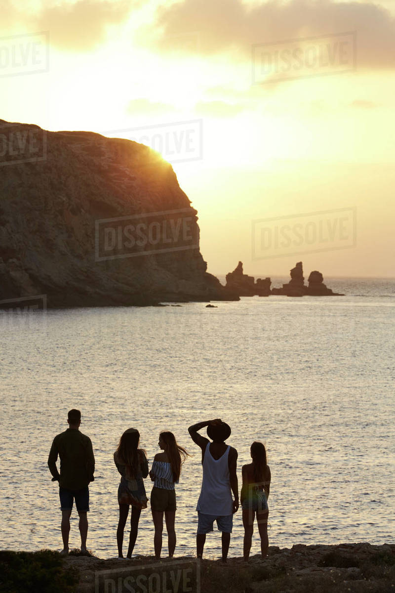 Rear View Of Friends Standing On Cliff Watching Sunset - Royalty-free ...