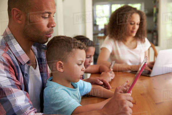 Family sitting around table at home using technology - Royalty-free ...
