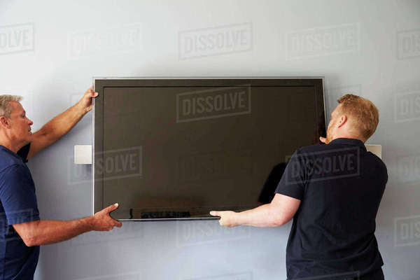 Two men fitting flat screen television to wall - Stock Photo - Dissolve