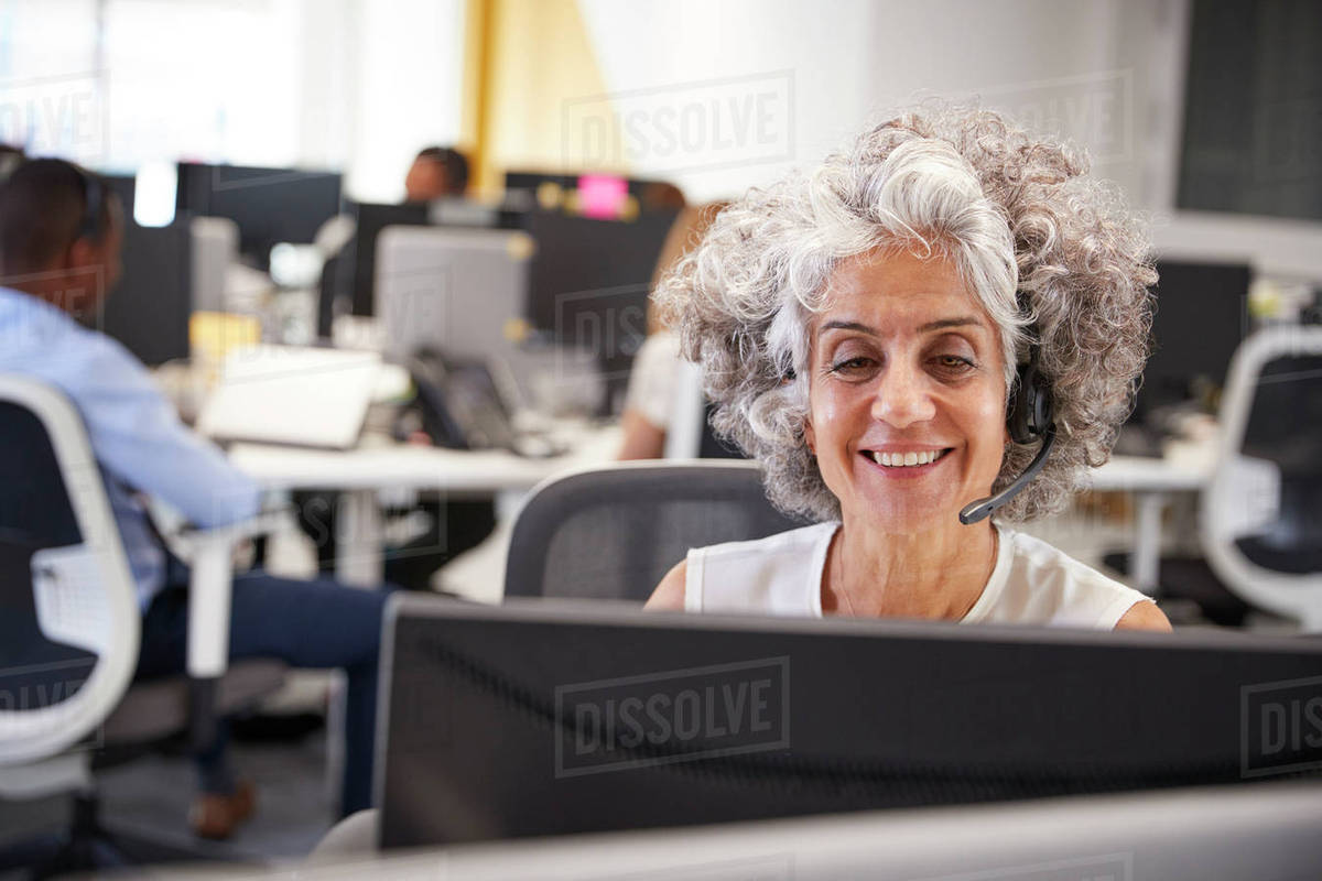 Middle aged woman working at computer with headset in office - Stock ...