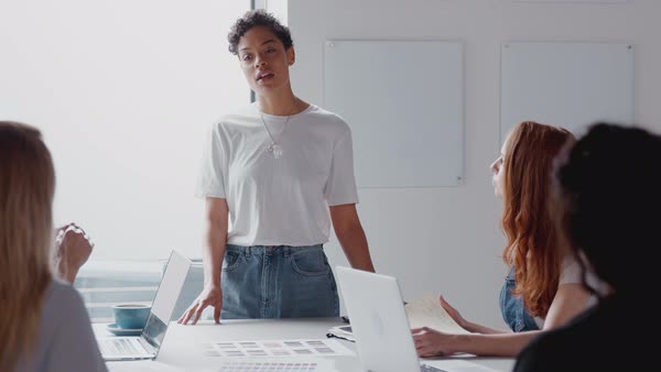Young female boss standing to give presentation to colleagues around ...