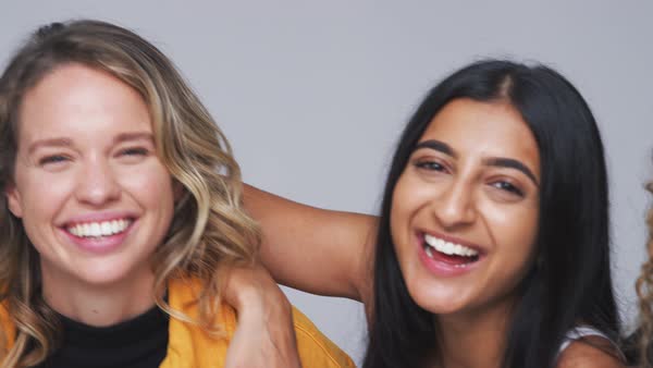 Camera tracks along faces of group of female friends in studio smiling ...