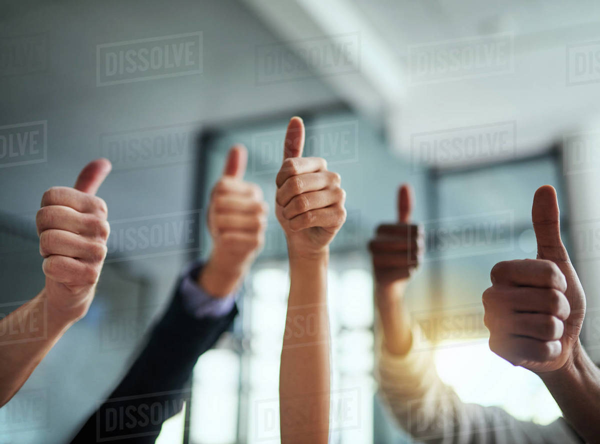 Closeup of business people showing thumbs up hand sign in a modern ...