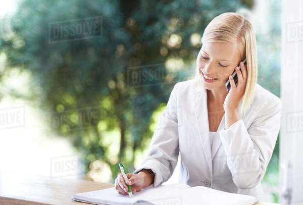Phone call, receptionist and woman writing notes at reception, talking ...