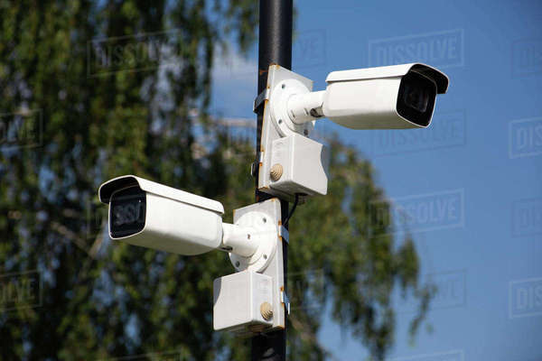 Two white surveillance cameras on a pole look in different directions ...