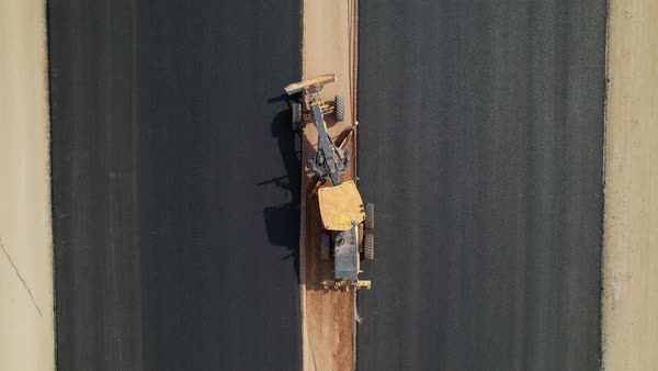 Construction grader levels the ground between an asphalt road for ...