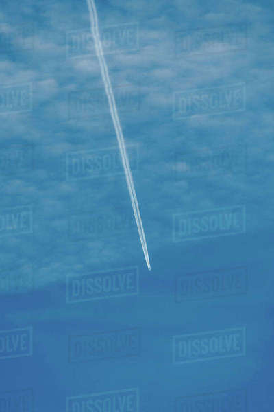Jet airplane flying in a blue sky with clouds forming long white ...