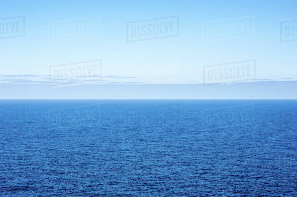 Expansive deep blue empty ocean seascape with layer of gray clouds ...