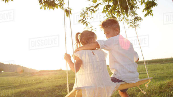 Couple children embracing on wooden swing at gold sunset. Young love ...