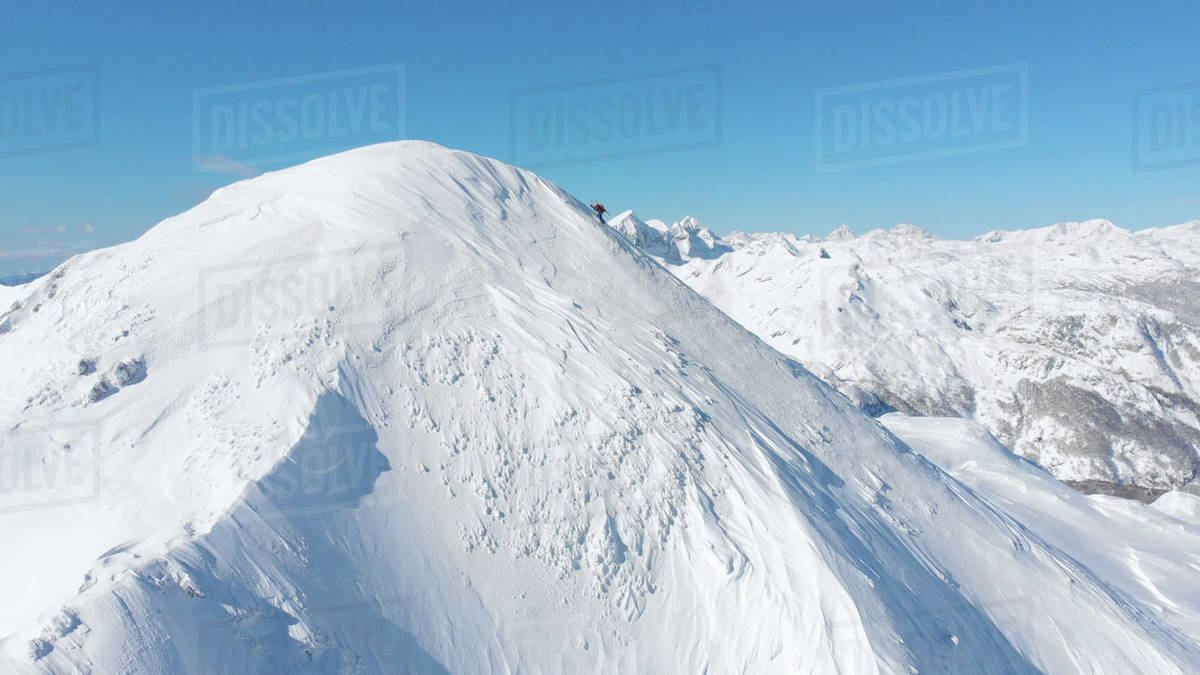 AERIAL: Unrecognizable skier hiking up the snowy mountain in sunny ...
