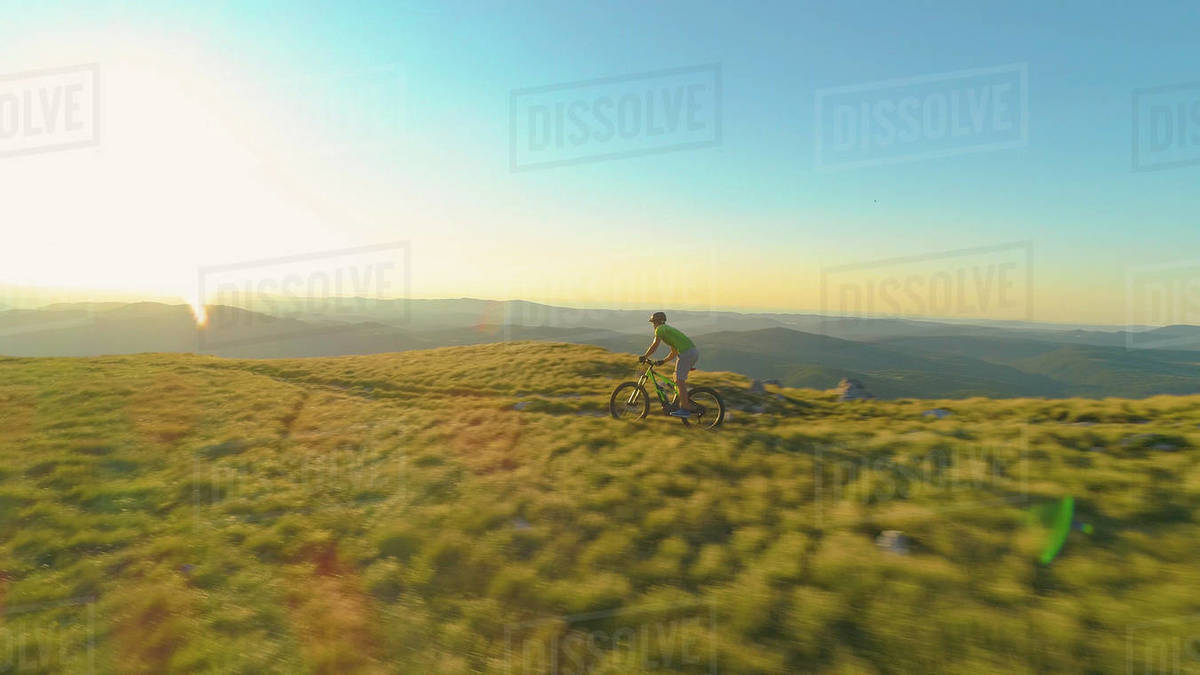 LENS FLARE, AERIAL: Flying behind an athletic man pedalling his ...