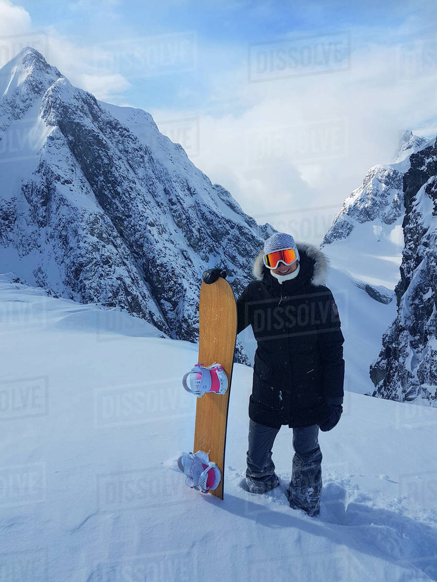 Excited snowboarder poses with her snowboard before riding down the ...