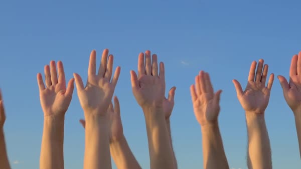 Slow motion of many hands raised against blue sky background ...