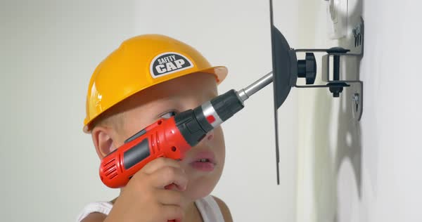 Little boy in yellow safety cap using toy screw gun to fix the holder ...