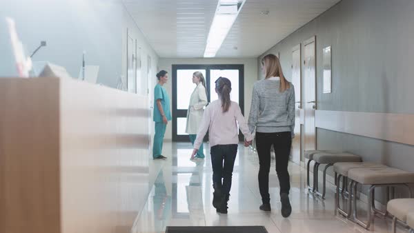 In the hopistal hallway nurses and doctors stand talking and mother and ...