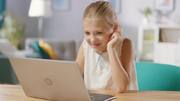 Cute little girl uses laptop while sitting at the desk in the living ...