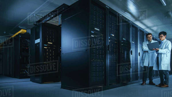 In the Data Center: Two IT Specialists Wearing White Lab Coats, Have ...