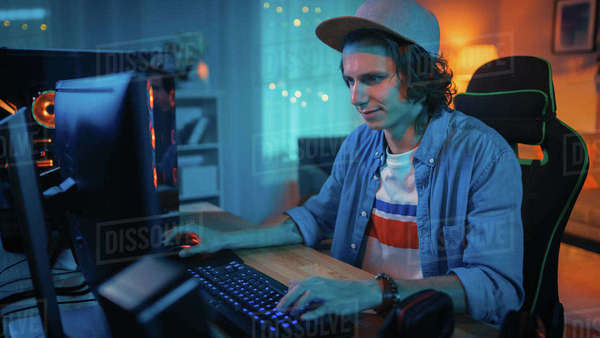 Excited gamer in cap playing online video game on his personal computer ...