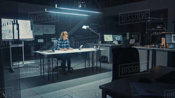 Female Engineer Sitting at Her Desk Works with Blueprints Laying on a ...