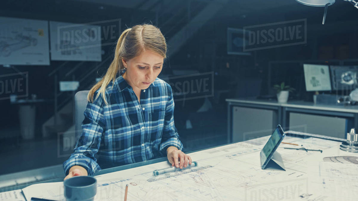 Female Engineer Sitting at Her Desk Works with Blueprints Laying on a ...