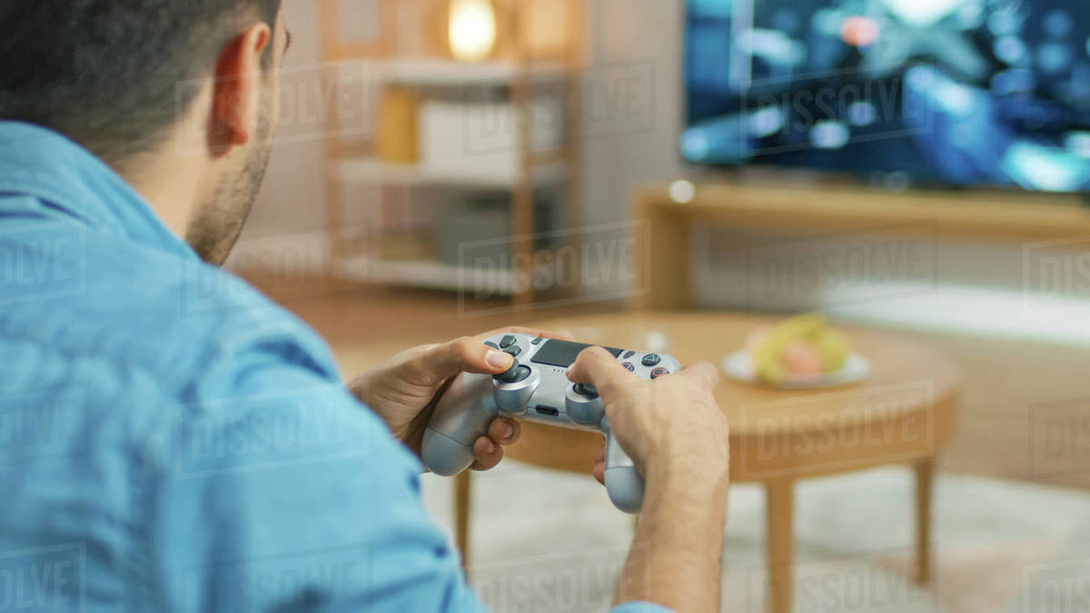 In the Living Room Man Sitting on a Couch Holds Controller Playing in a ...