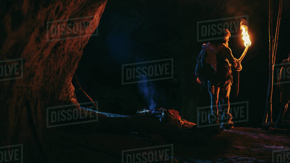 Primeval Caveman Wearing Animal Skin Stands in a Cave At Night, Holding ...