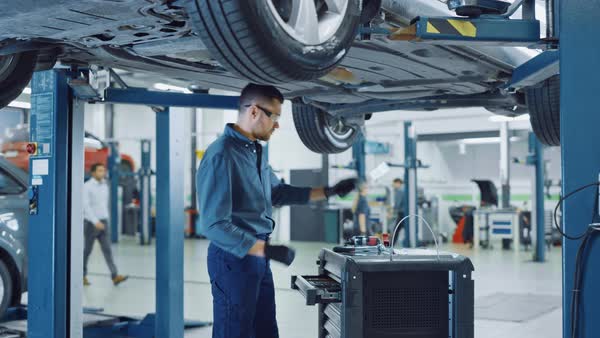 Handsome Professional Car Mechanic is Working Under a Vehicle on a Lift ...