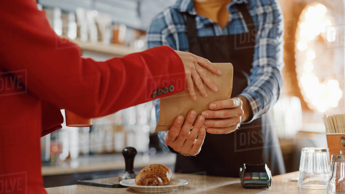 Close-up view of a barista handing a customer an order at a coffee shop ...