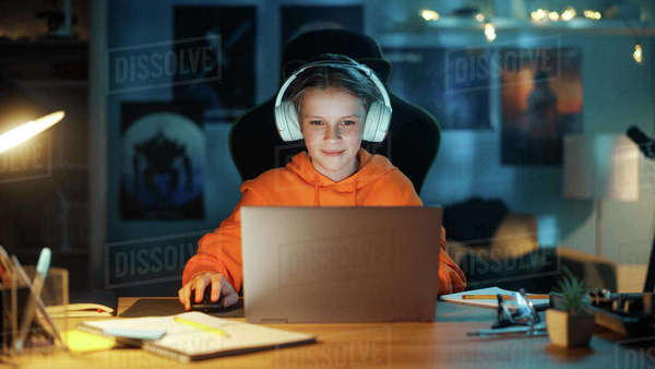 Young Boy in Headphones Using Laptop Computer in Cozy Dark Room at Home ...