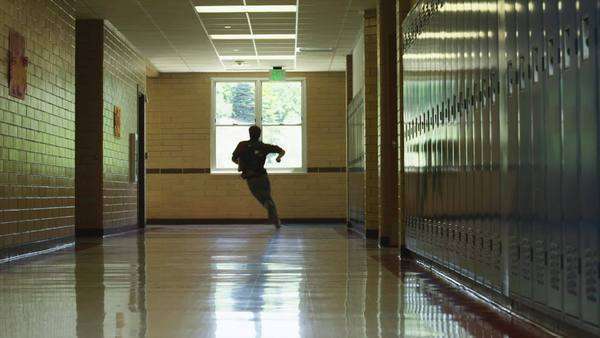 Wide shot schoolboy (16-17) running down school corridor / Spanish fork ...