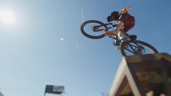 Low angle tracking shot of boy jumping wooden ramp on bicycle at bike ...