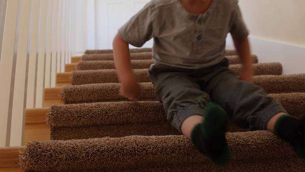 An adorable little boy bounces down the stairs while sliding on his bum ...