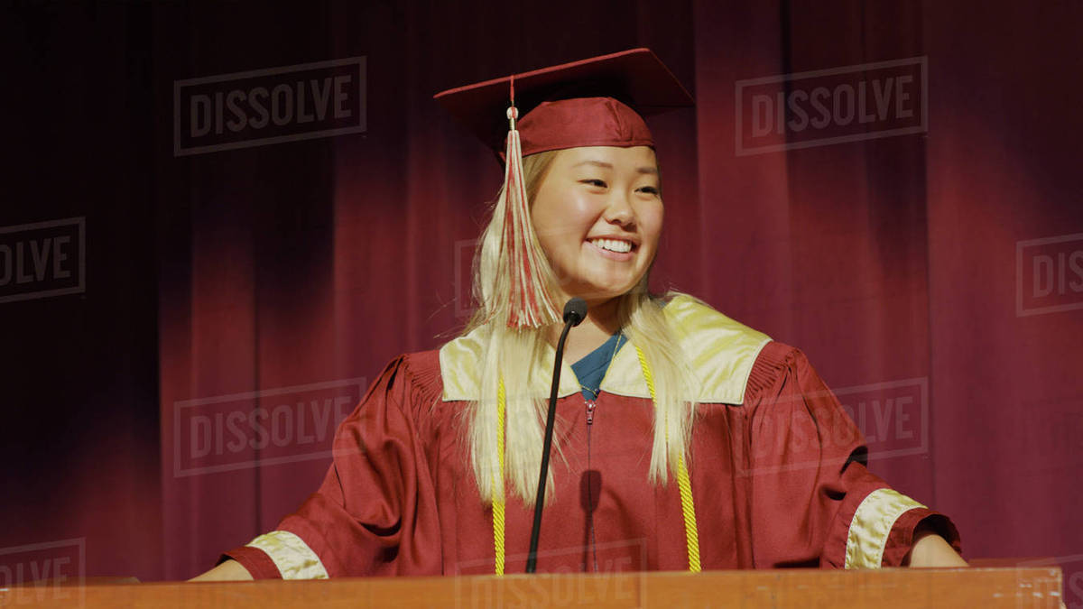 Smiling student speaking at podium on stage during graduation ceremony ...