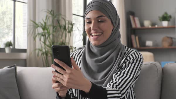 Happy smiling muslim woman holds mobile smart phone makes a video call ...