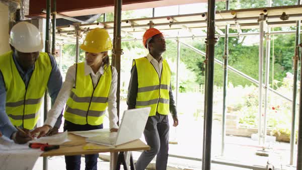 Architects with laptop at construction site and building crew working ...