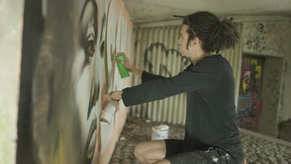 Masked graffiti artist creating portrait of a woman's face on city wall ...
