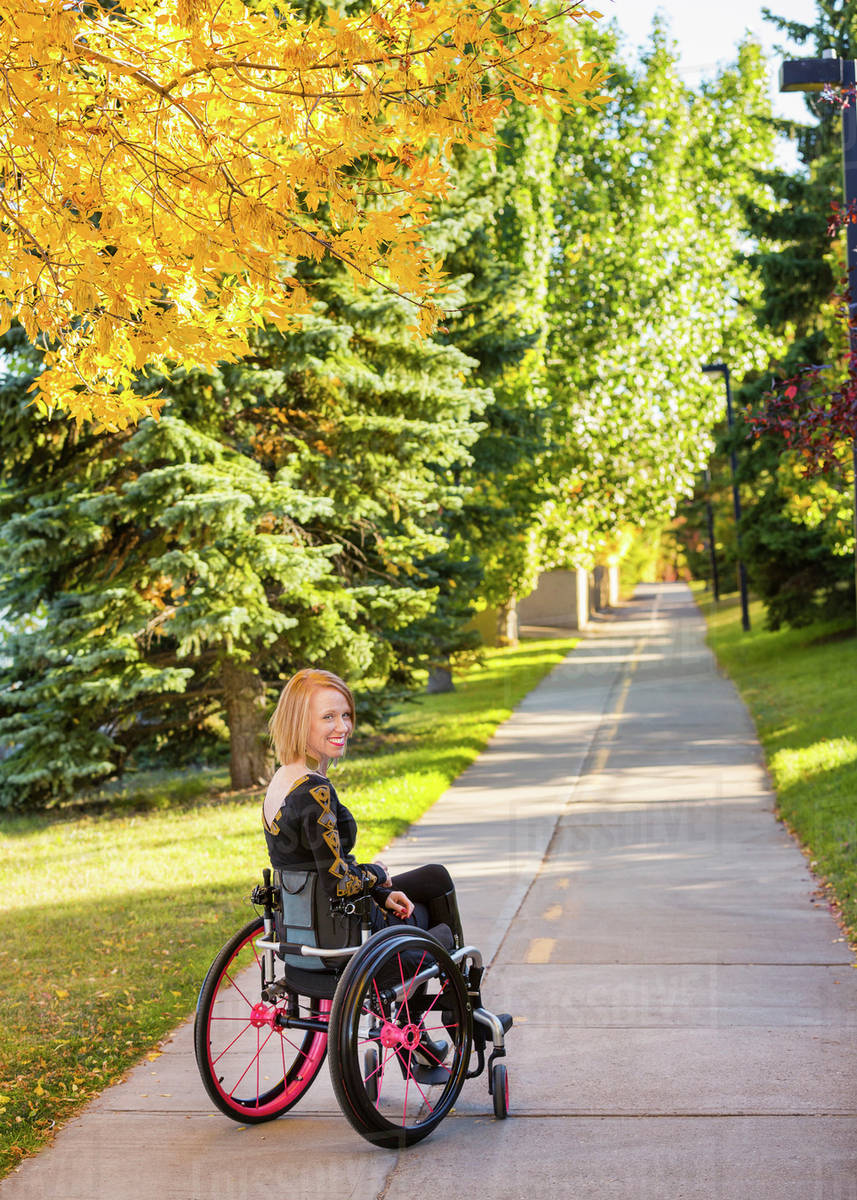 Young paraplegic woman in her wheelchair on a path in a city park in ...