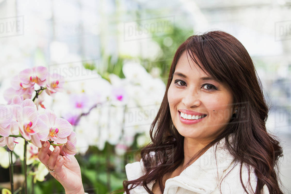 Young woman looking at flowers in a greenhouse; St. Albert, Alberta ...