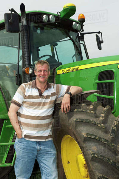 Agriculture - A farmer leans on the tire of his John Deere tractor ...