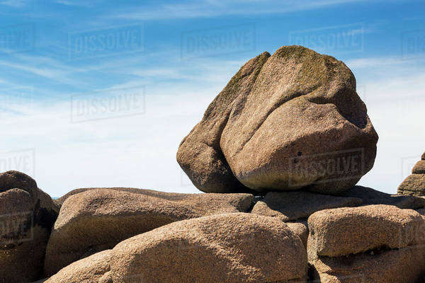 Large round rock balanced on rock formation with blue sky and clouds ...