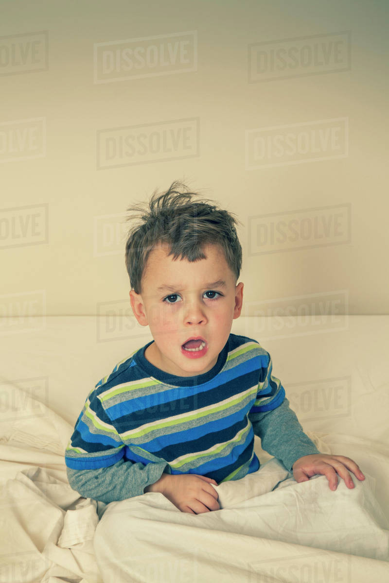 Young boy sitting in bed complaining; Connecticut, United States of ...