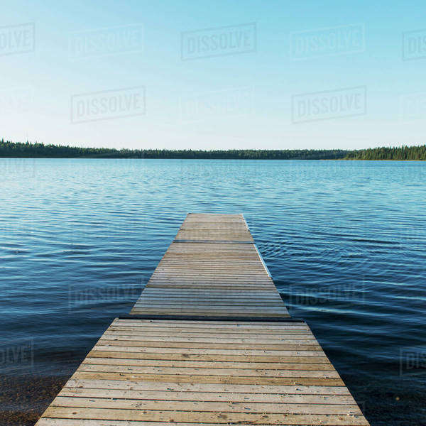 A wooden dock leading out to a lake and blue sky in Riding Mountain ...