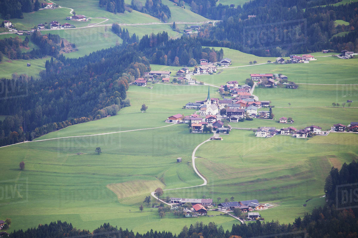 View of an alpine village with green meadows, rolling hills and trees ...