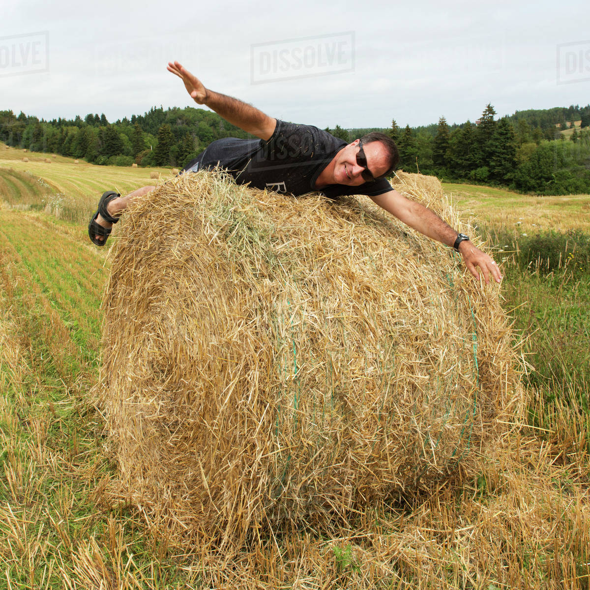 A man lays in a silly pose on top of a large hay bale; Kensington ...