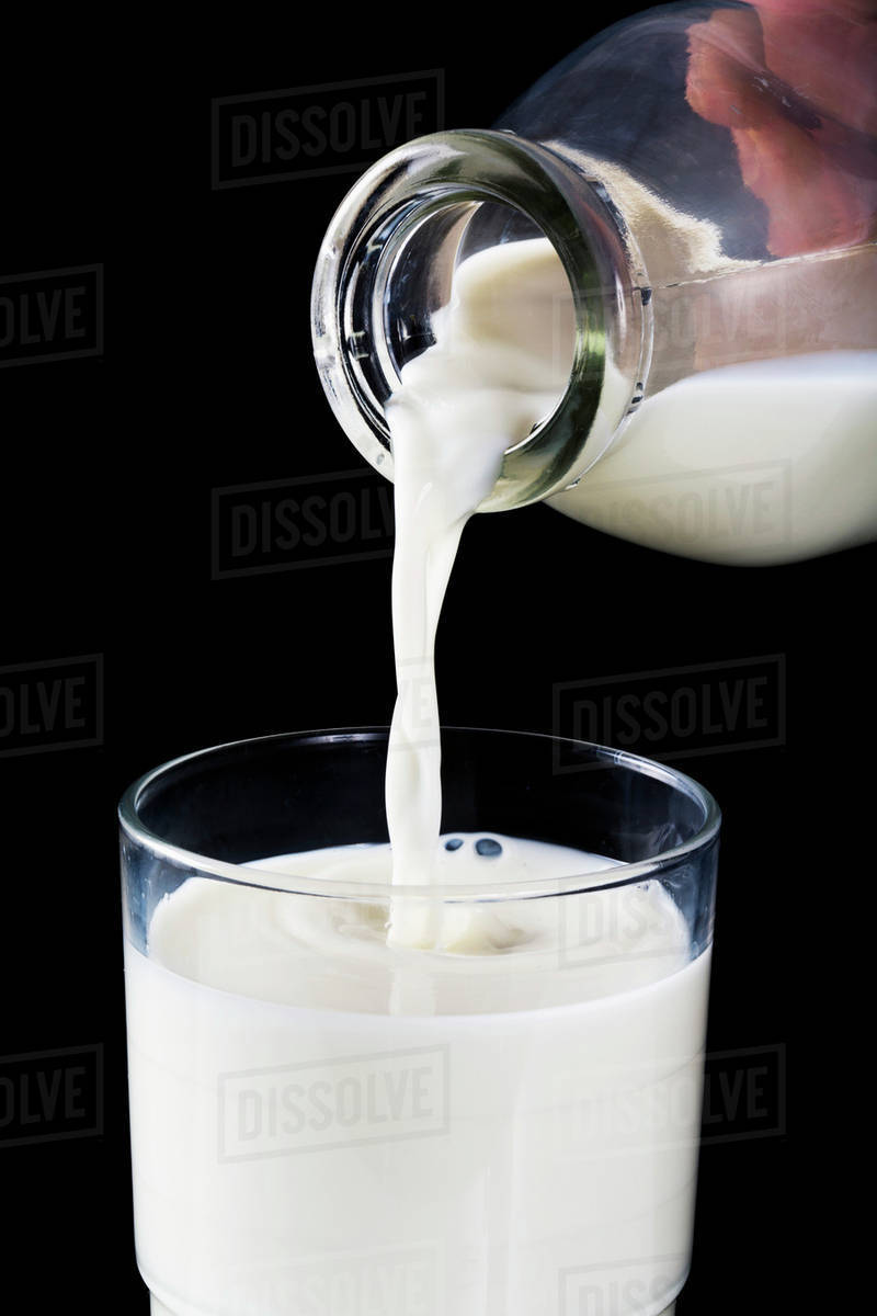 Glass bottle of milk being poured into glass with black background ...