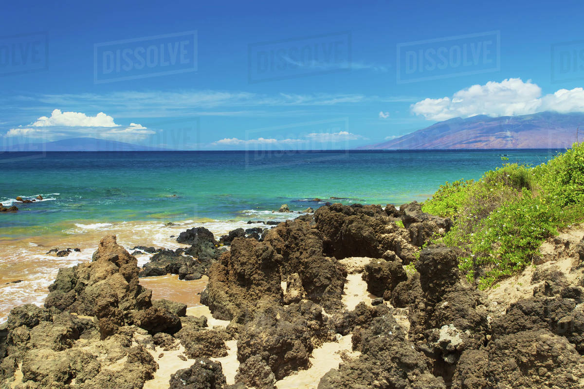 Rugged rocks sitting on the sand on the shore of an hawaiian island ...