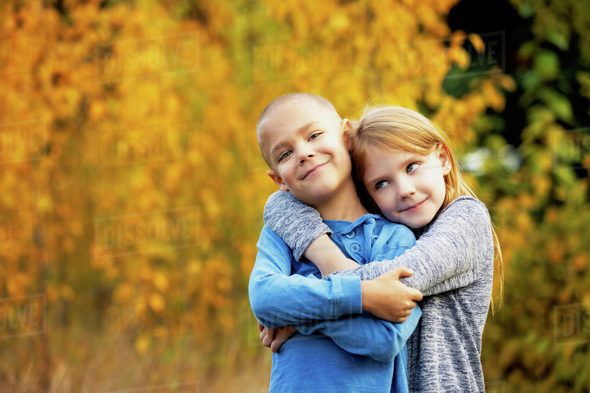 Outdoor portrait of a brother and sister in an embrace in a park area ...
